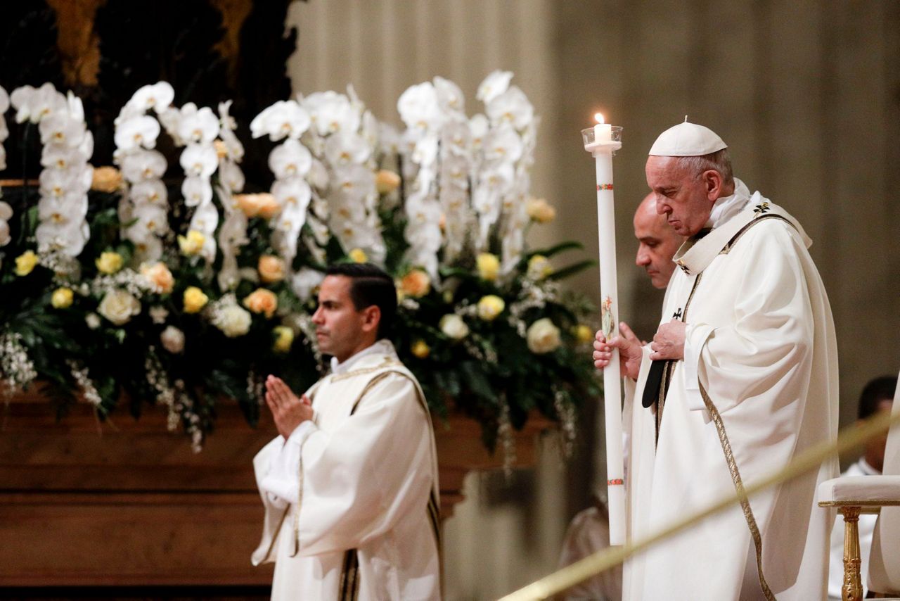 Pope carries Easter candle up aisle of darkened basilica