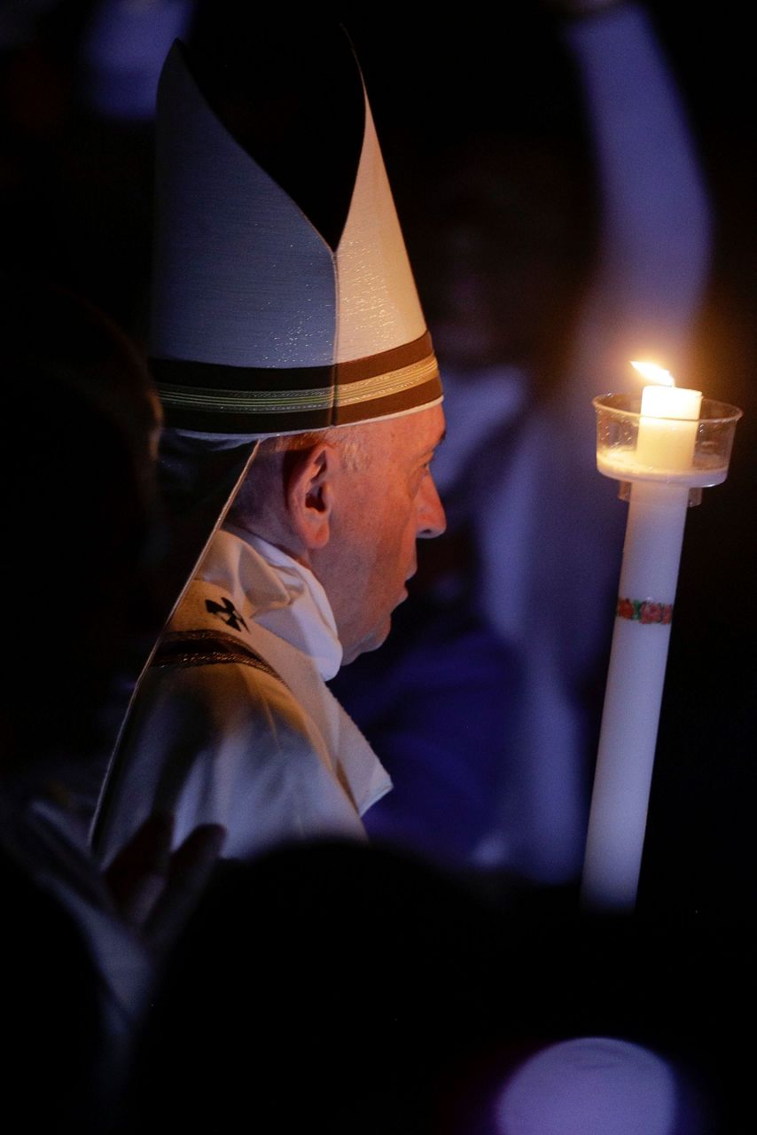Pope carries Easter candle up aisle of darkened basilica
