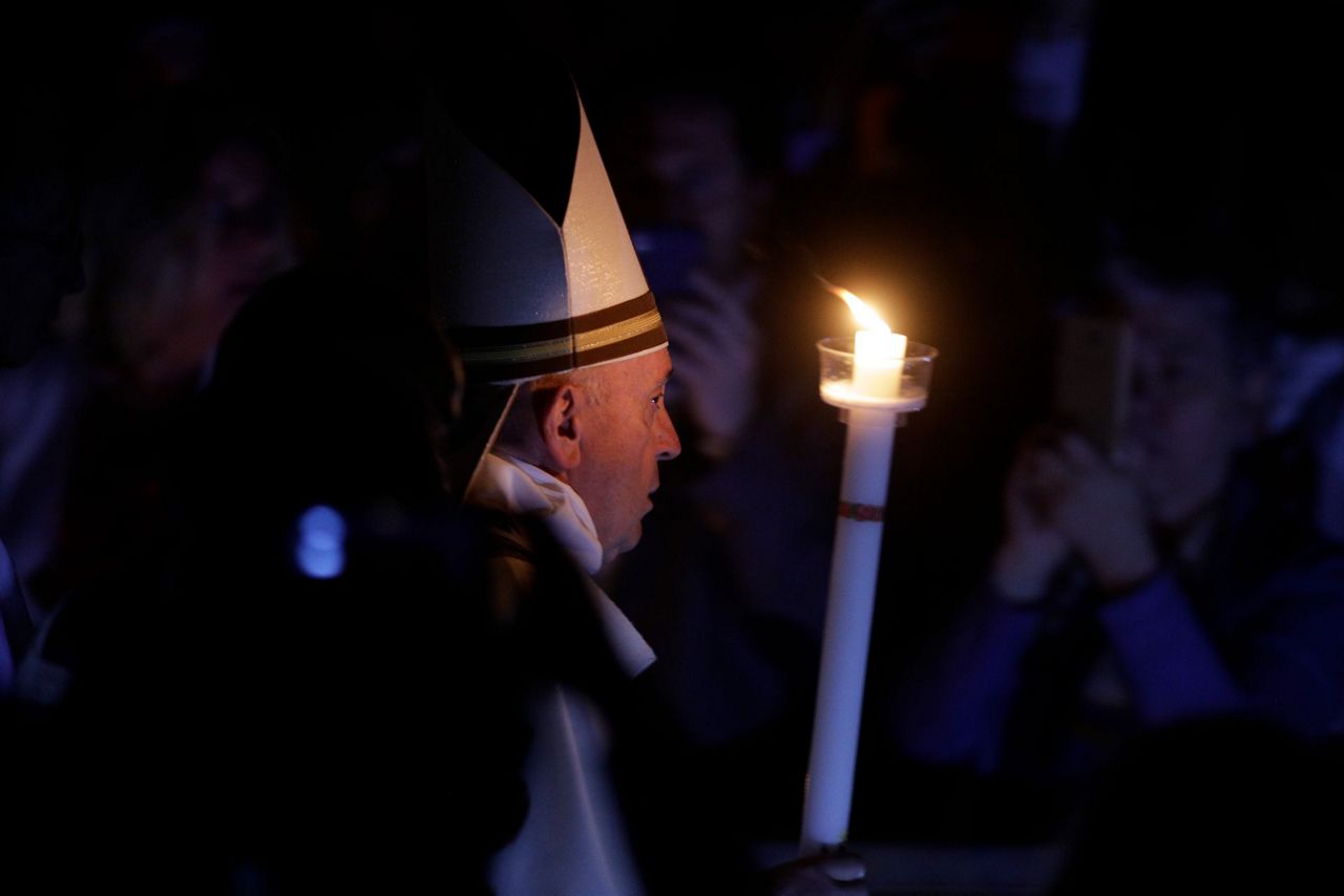 Pope carries Easter candle up aisle of darkened basilica